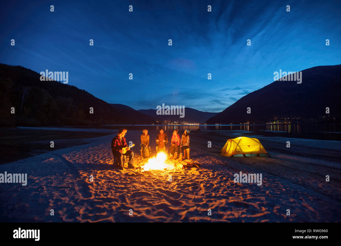 Group of friends around evening campfire at Troupe beach in nelson BC ...