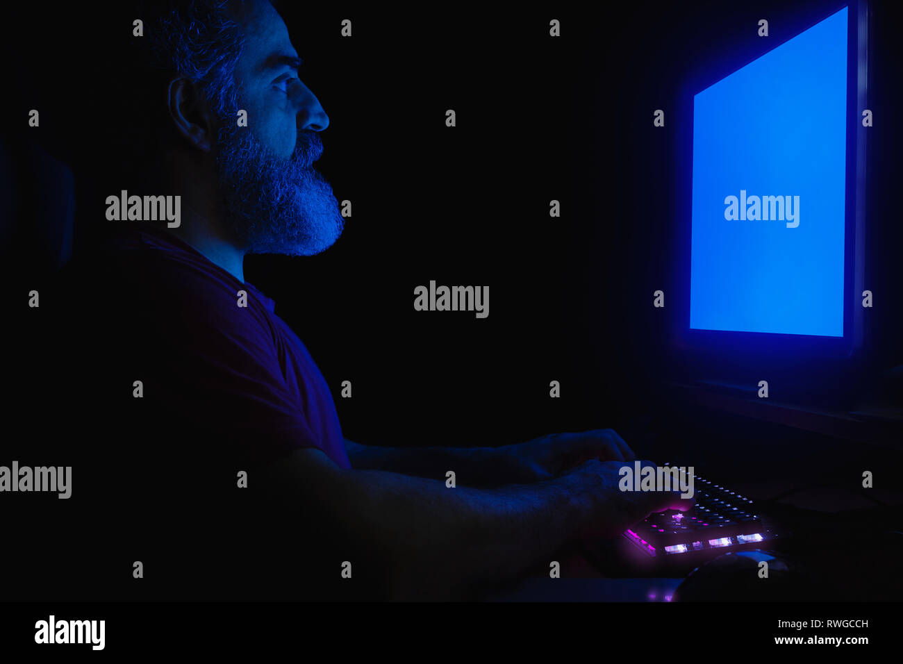 Bearded man sitting in front of computer monitor, hands on a keyboard ...