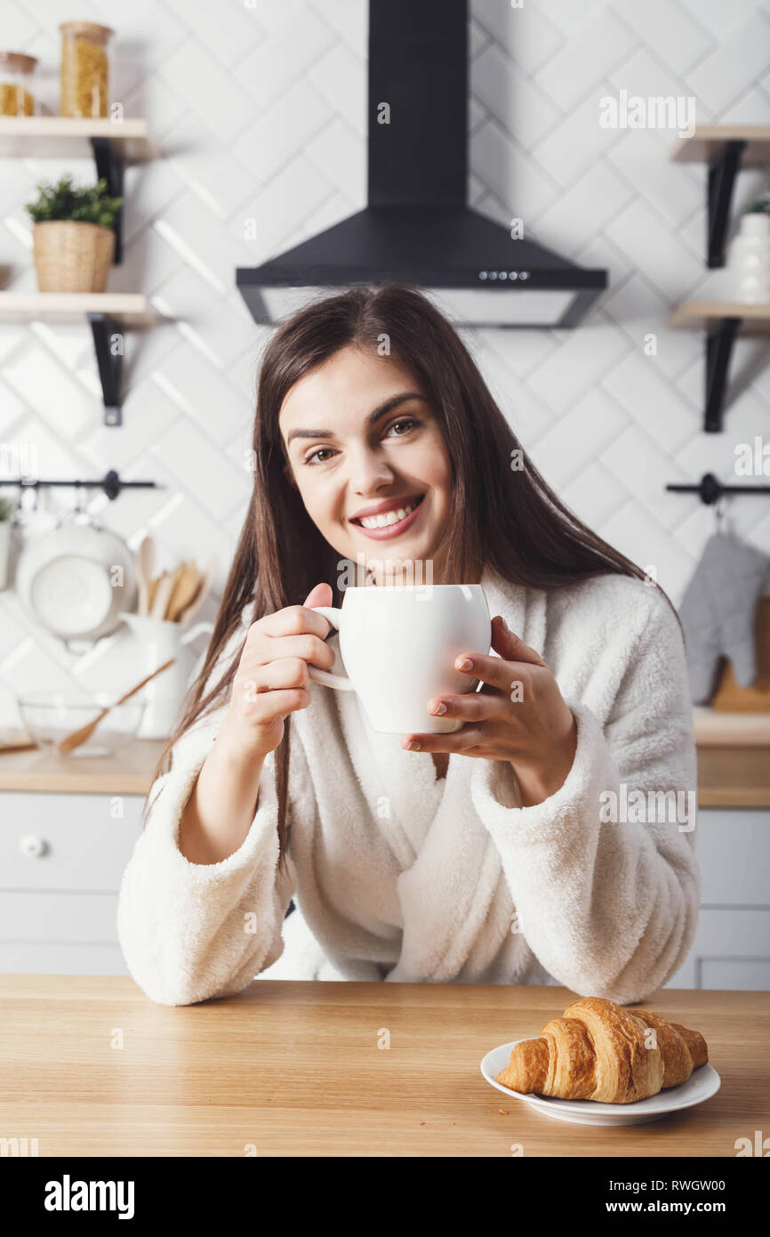 Happy girl having breakfast in the kitchen with croissants and coffee ...