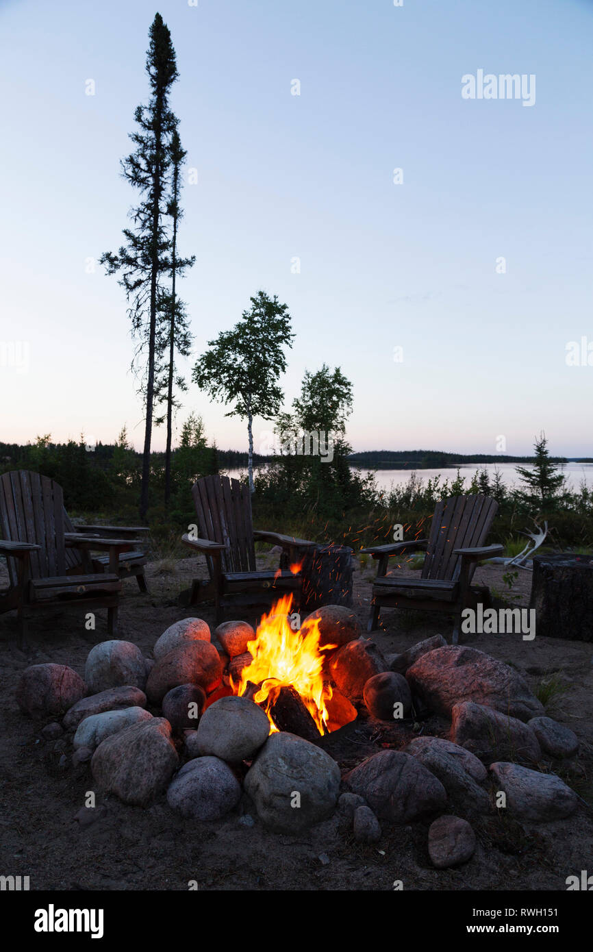 Chairs surround the flames of a campfire at a fishing camp in northern ...