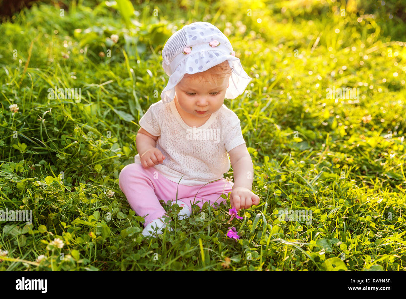 Sweet happy little baby girl sitting on grass in park, garden, meadow ...