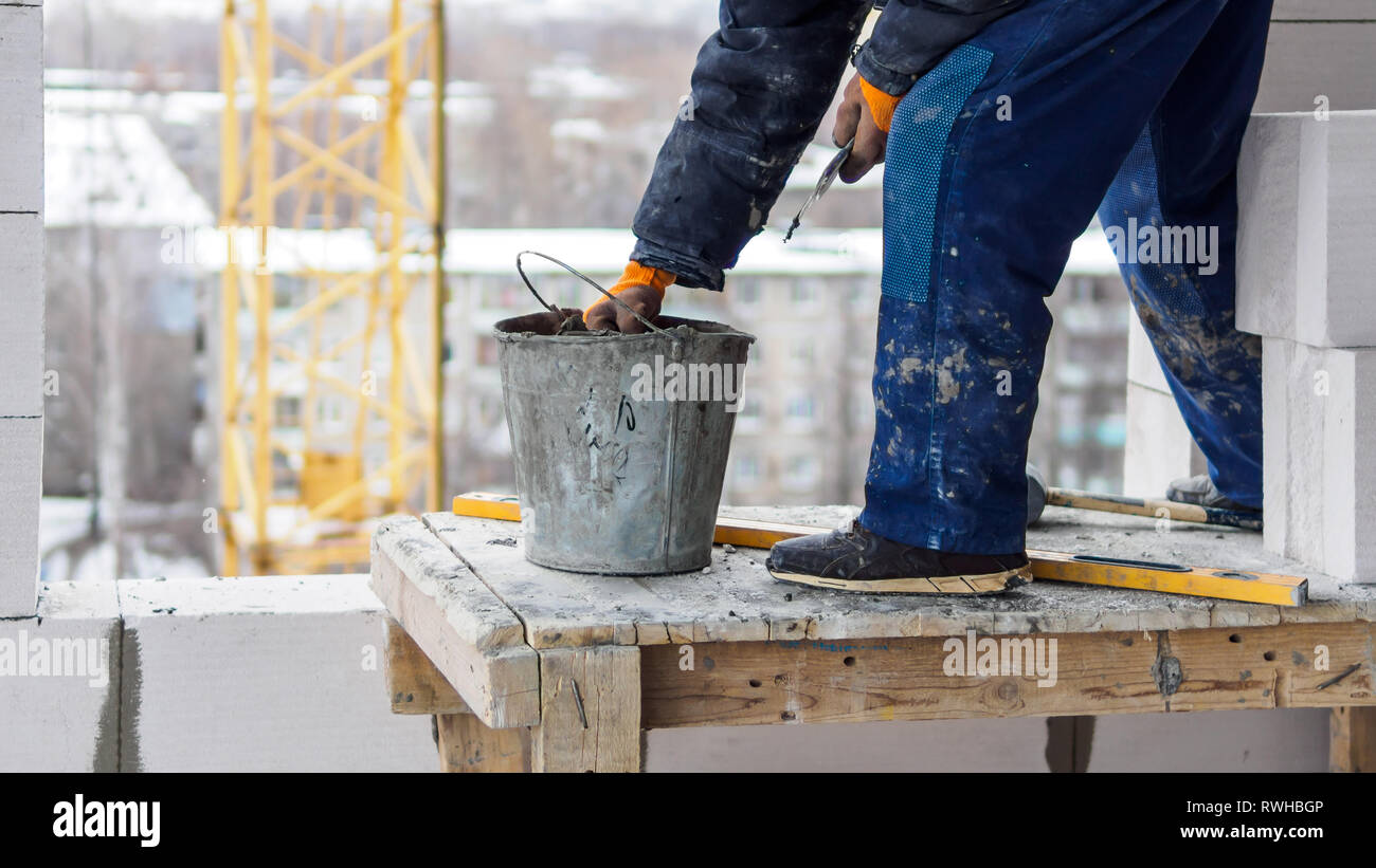 Professional worker laying brick in building construction. Yellow crane ...