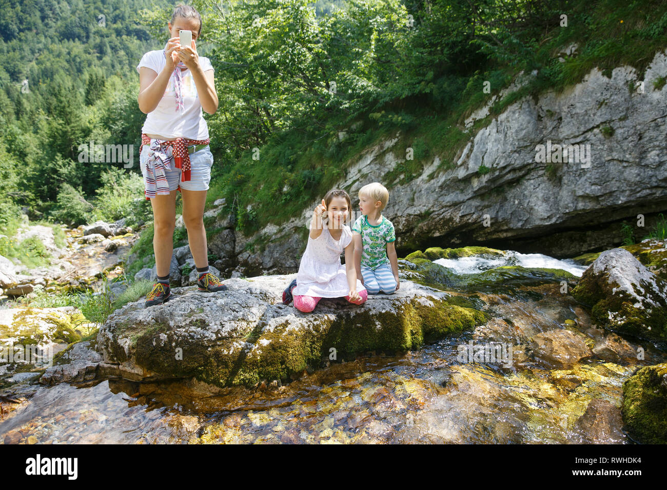 Mother taking a snapshot on a family trip with kids by a mountain ...