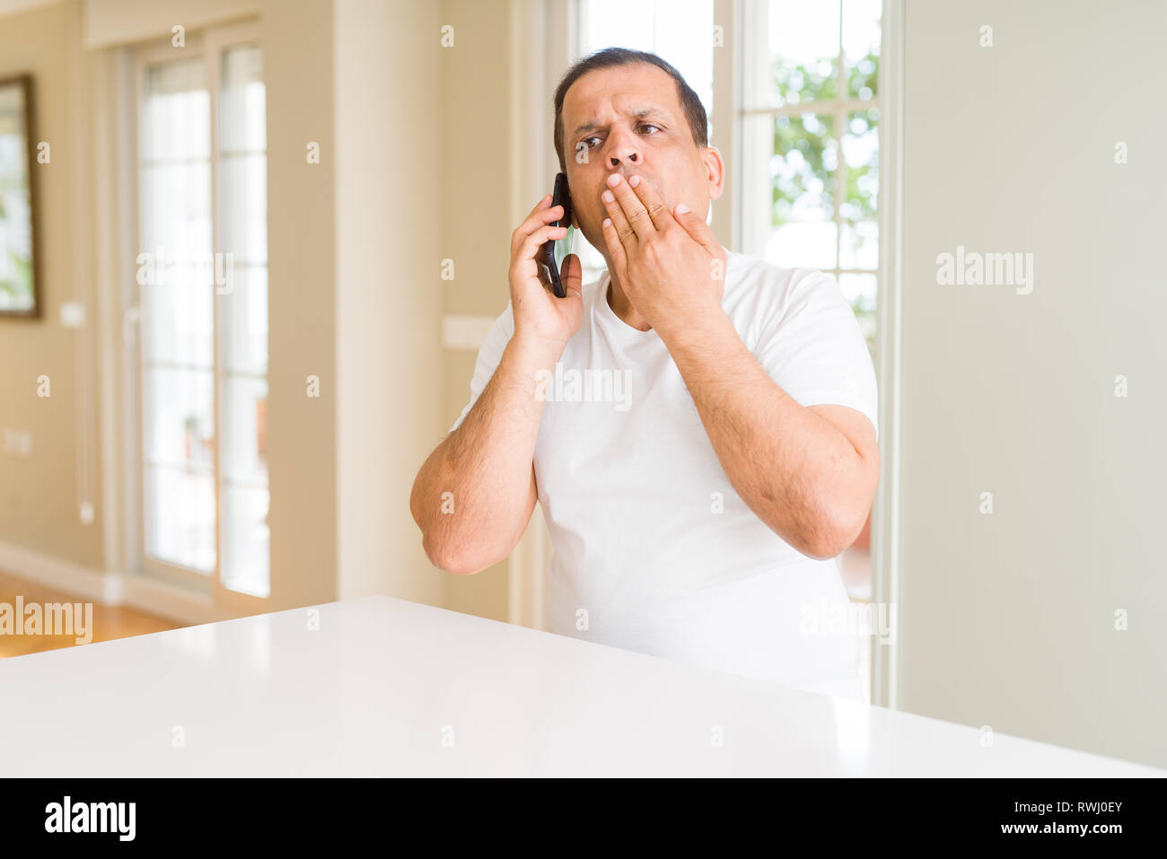 Middle age man calling using smartphone cover mouth with hand shocked ...