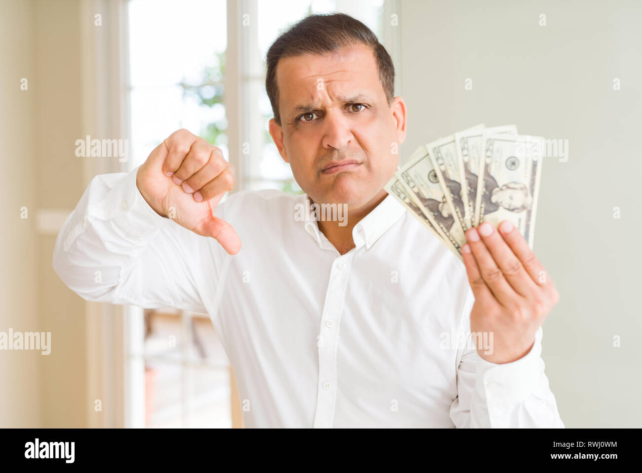 Middle age man holding bunch of dollars with angry face, negative sign ...