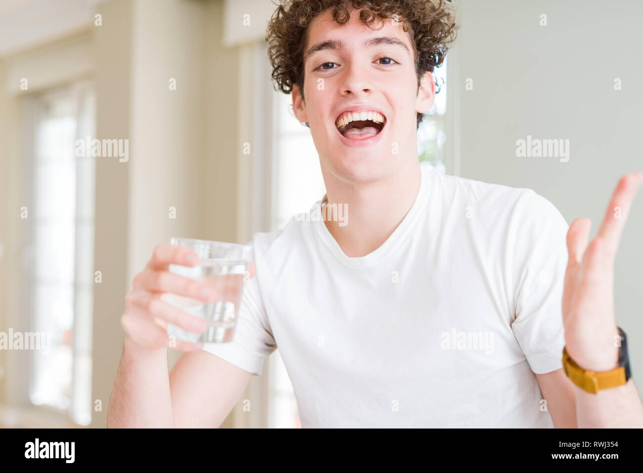 Young man drinking a glass of water at home very happy and excited ...