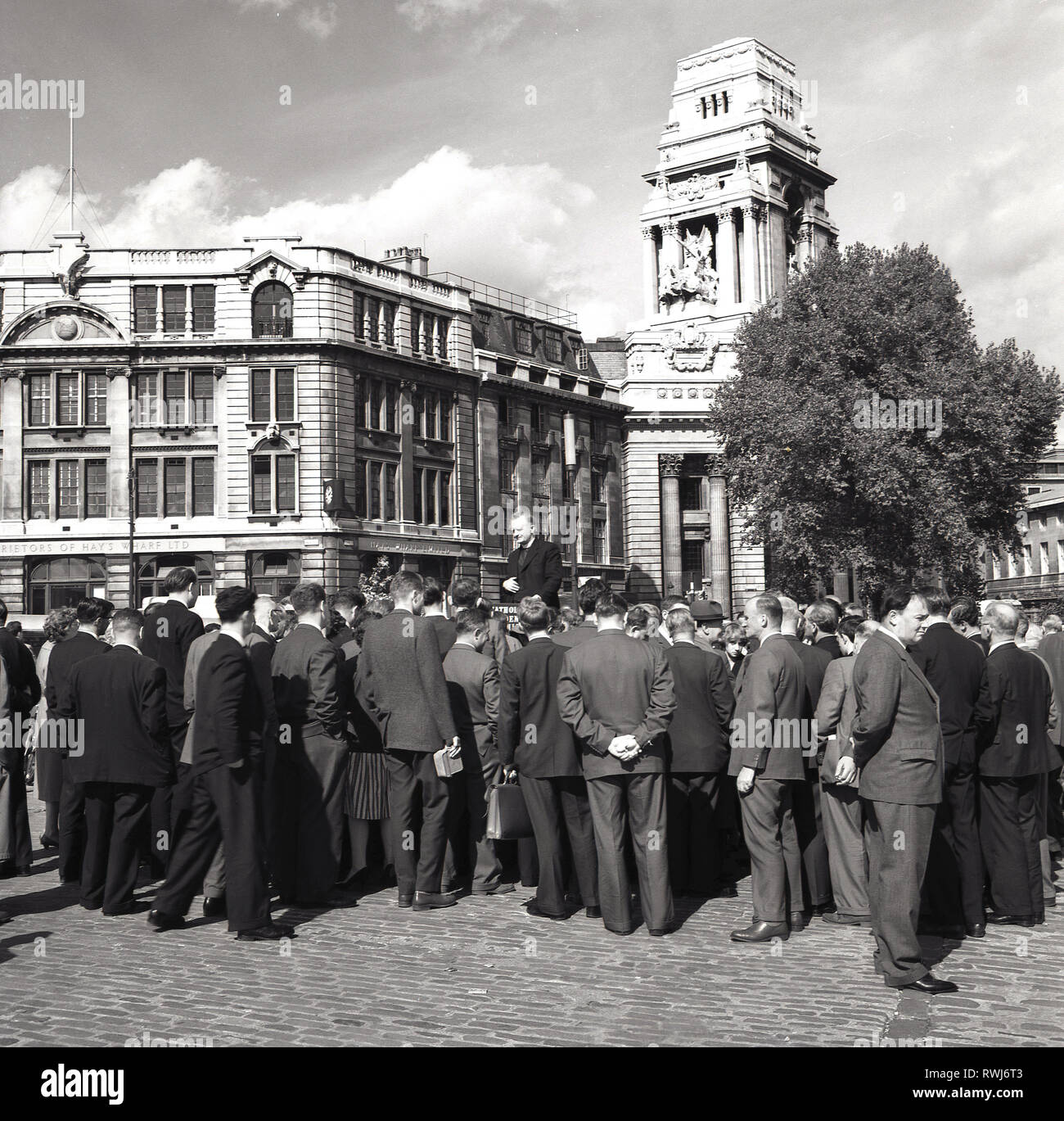 1950s, lunchtime and a crowd of city men in suits gather to watch and ...