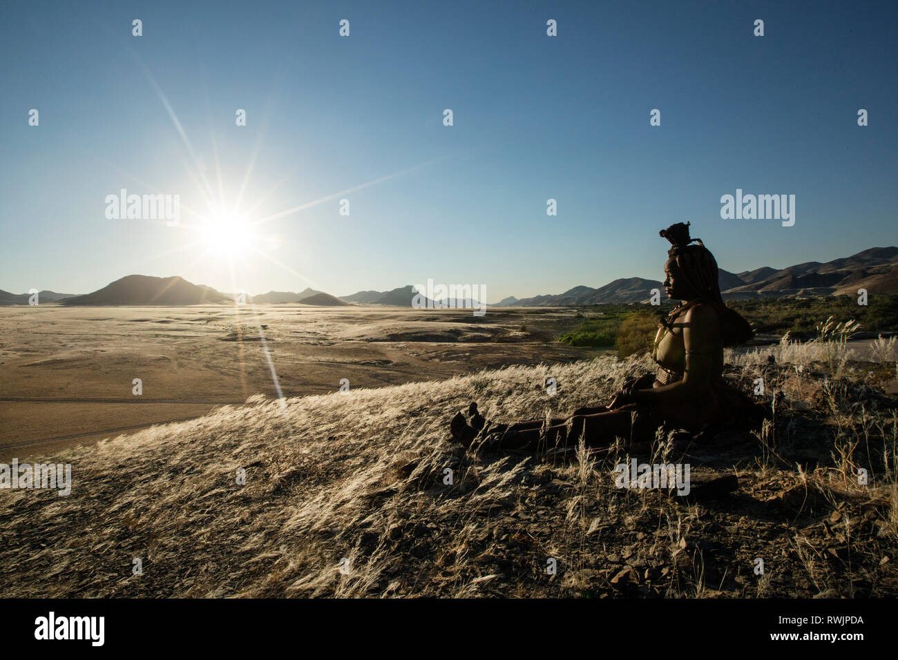 A Himba woman sits on top of a hill near Purros, Namibia Stock Photo ...
