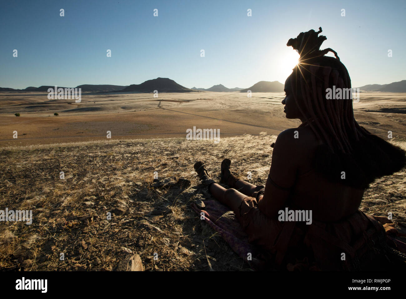 A Himba woman sits on top of a hill near Purros, Namibia Stock Photo ...