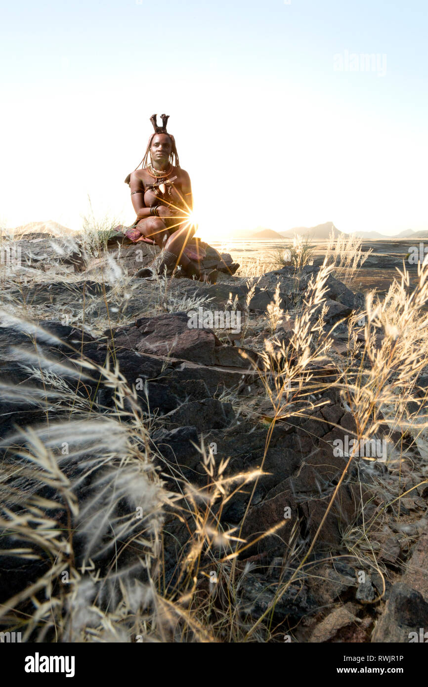 A Himba woman sits on top of a hill near Purros, Namibia Stock Photo ...