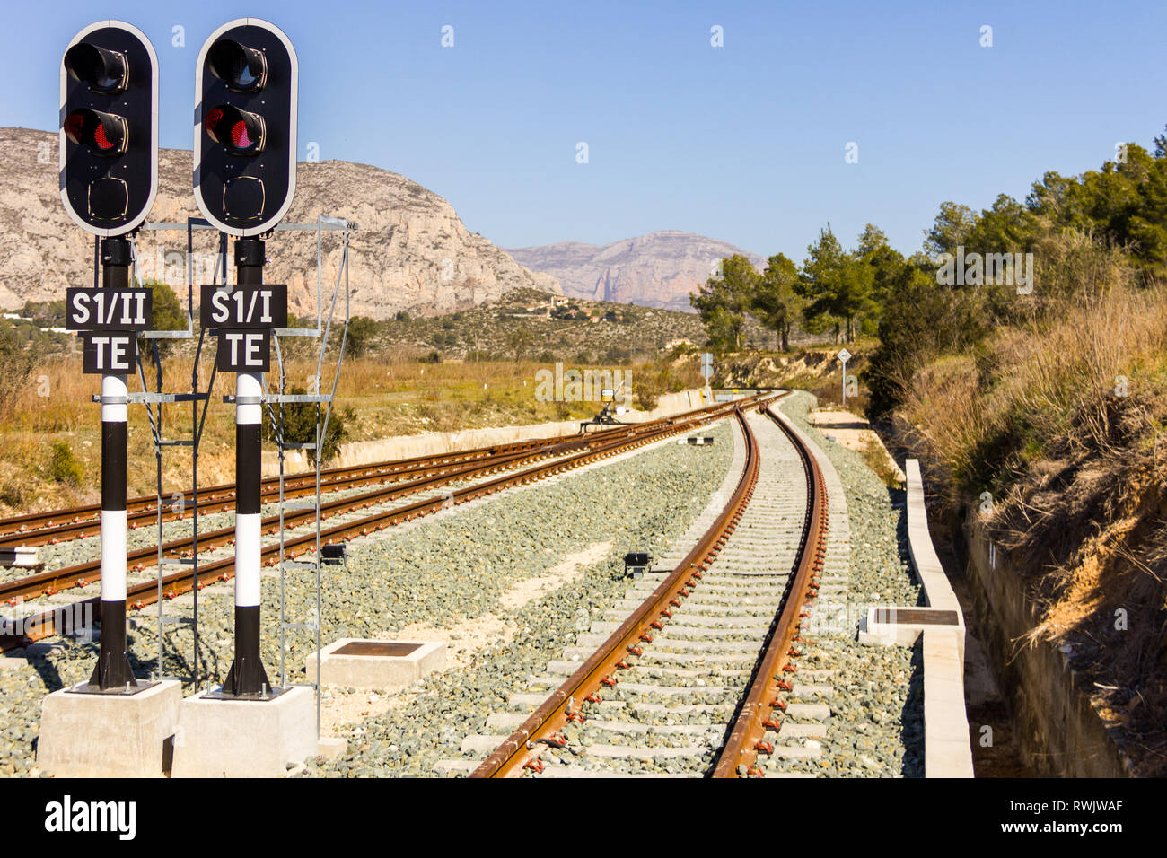 A railroad switch track with traffic lights, mountains and trees in the ...