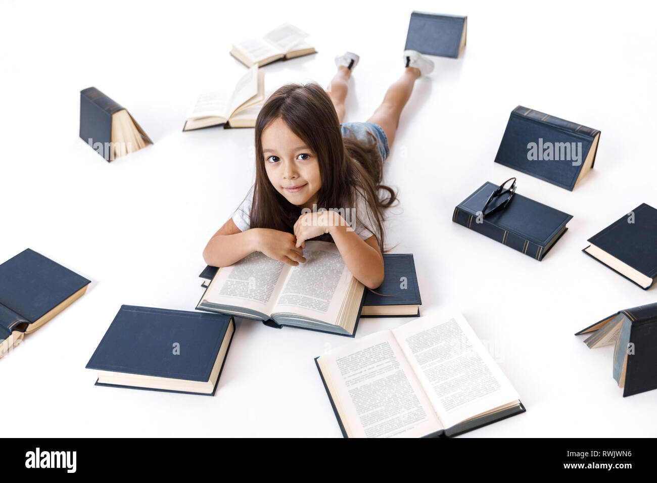 cute little girl in denim is reading a book. child and a lot of books ...