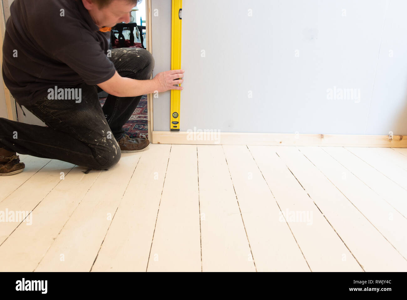 Workman checking skirting board for levelness Stock Photo - Alamy