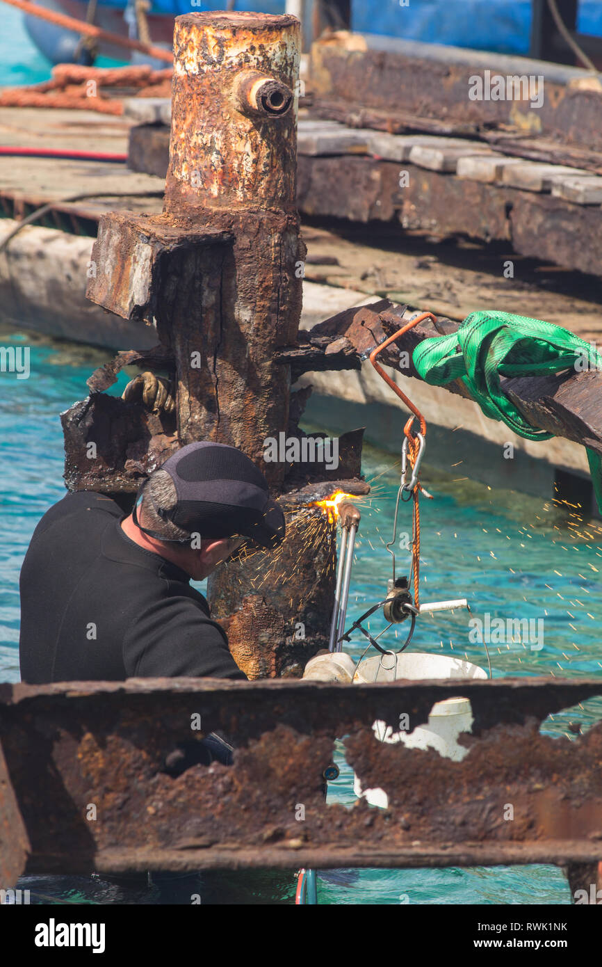 Men at work: worker deconstructing an old and broken steel pier ...