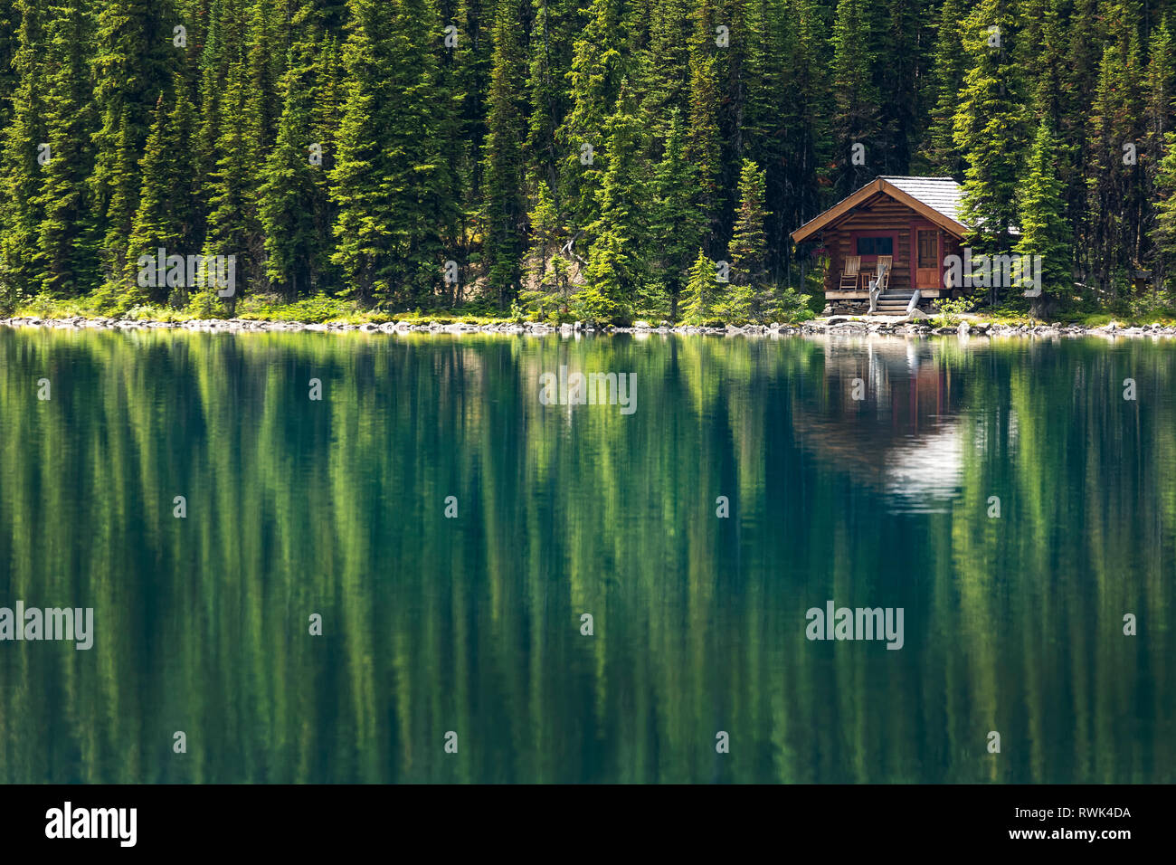 Log cabin amongst evergreen trees along an alpine lake shoreline with ...