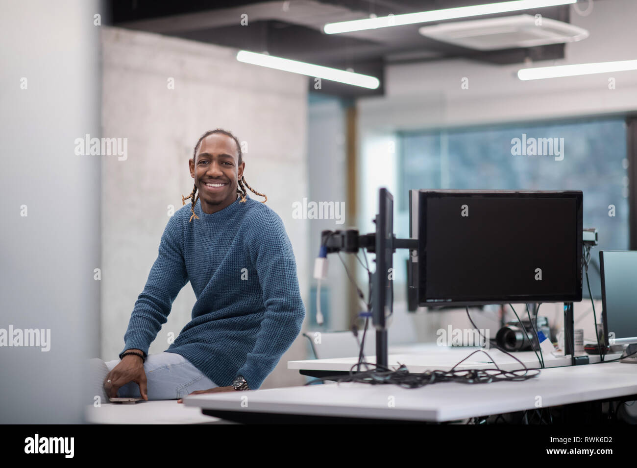 Portrait of young smiling african american male software developer sitting on office desk at ...