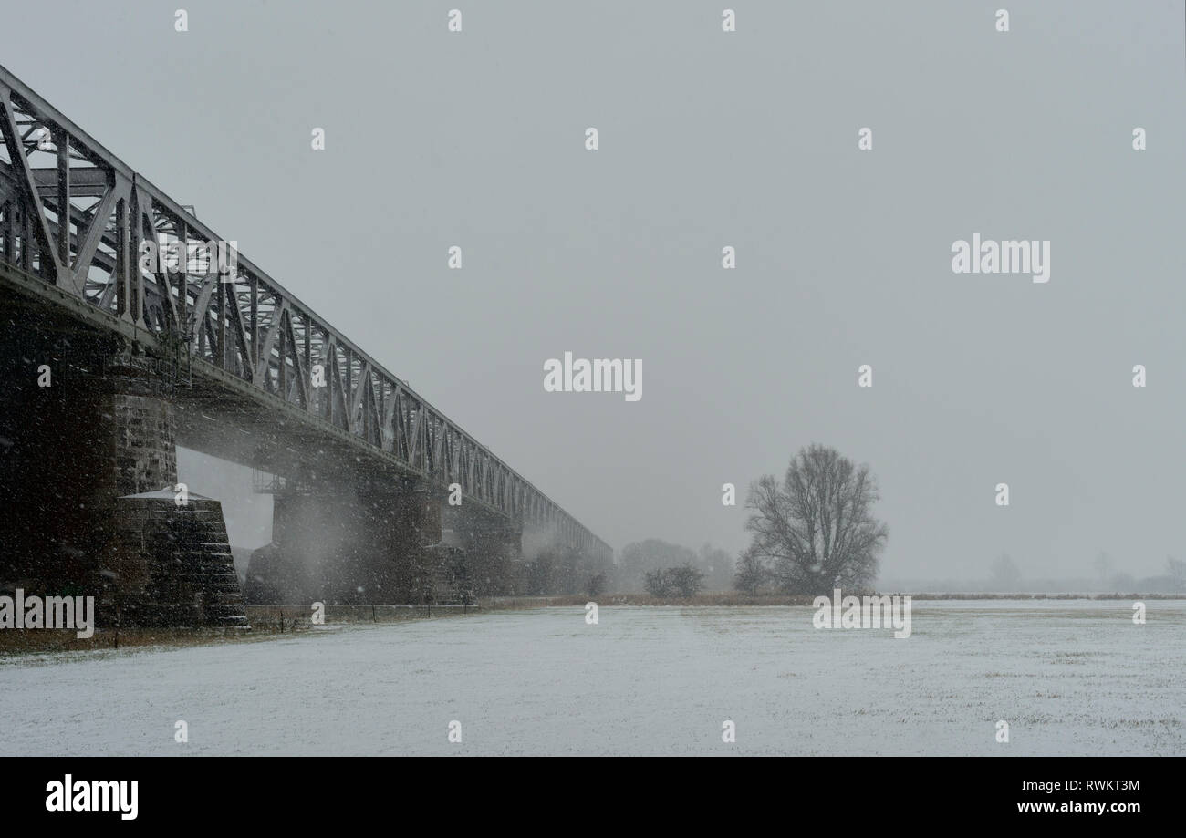 Old railway bridge running over floodlands of river Maas on snowy day ...