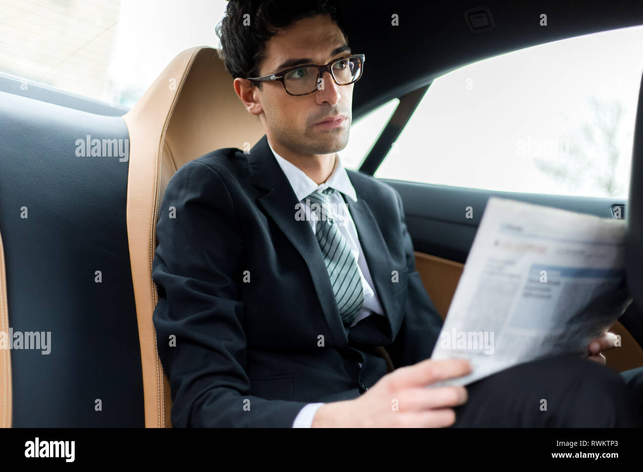 Young manager reading a newspaper in the back seat of a car Stock Photo ...