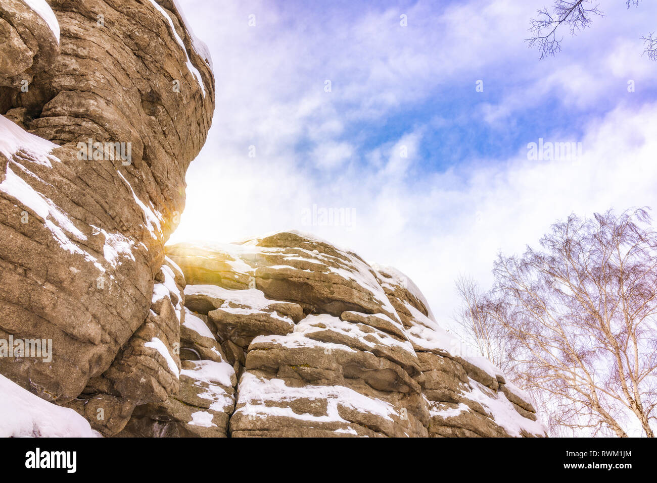 Granite layered rocks covered with snow against the blue sky. The sun ...
