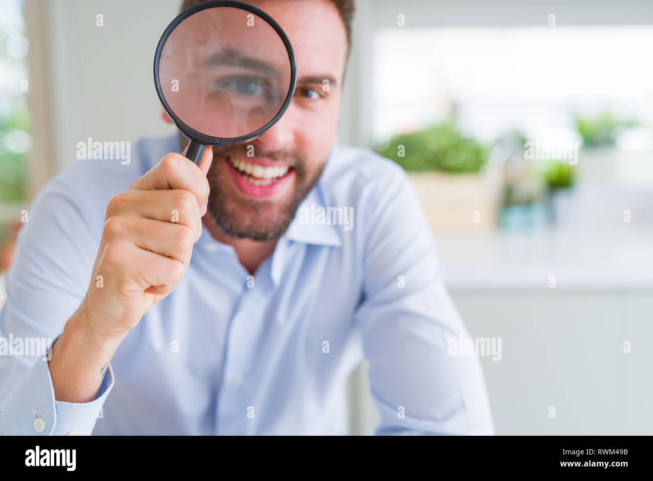 Handsome business man holding magnifying glass close to face, big eyes ...