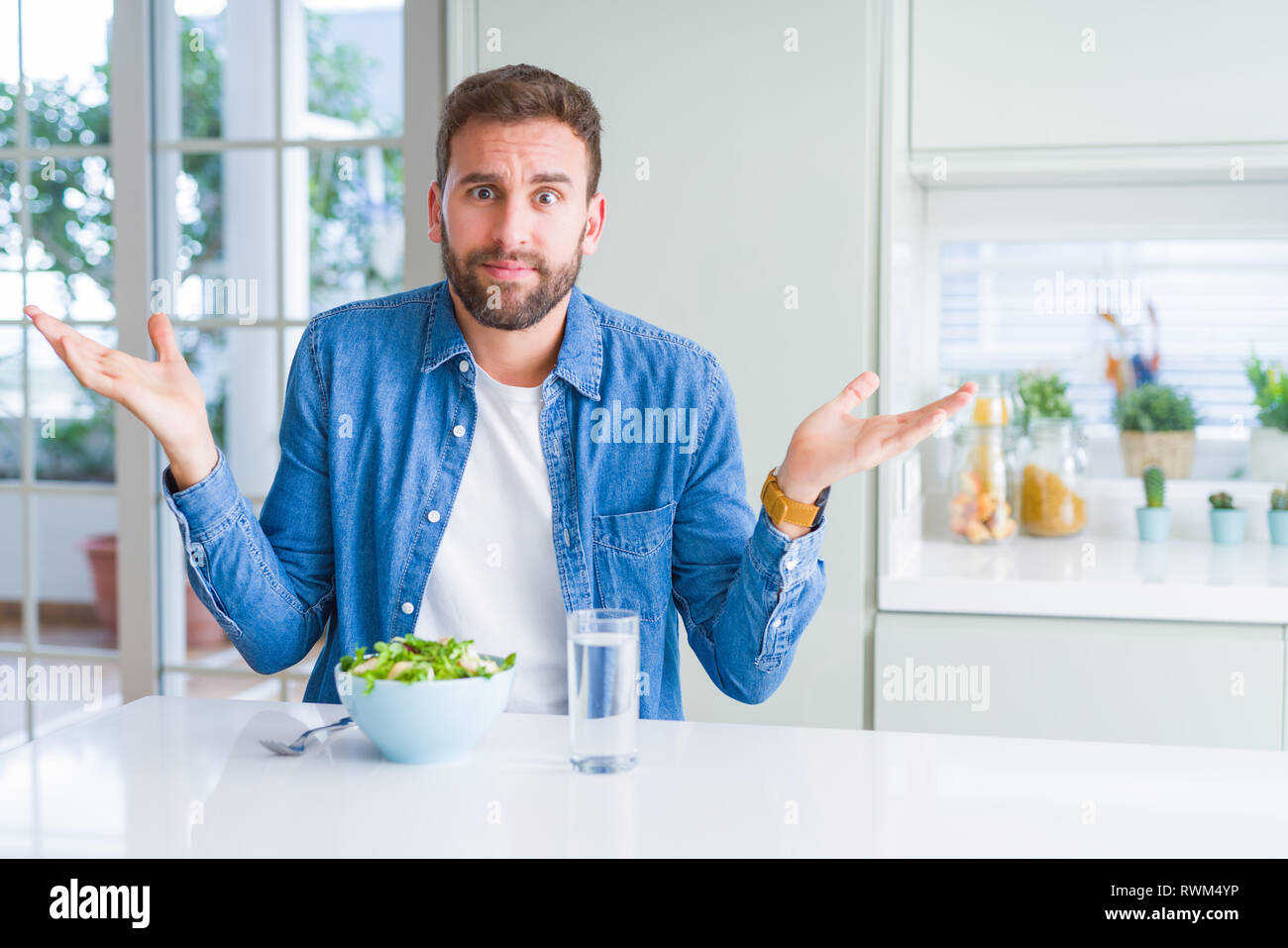 Handsome man eating fresh healthy salad clueless and confused ...