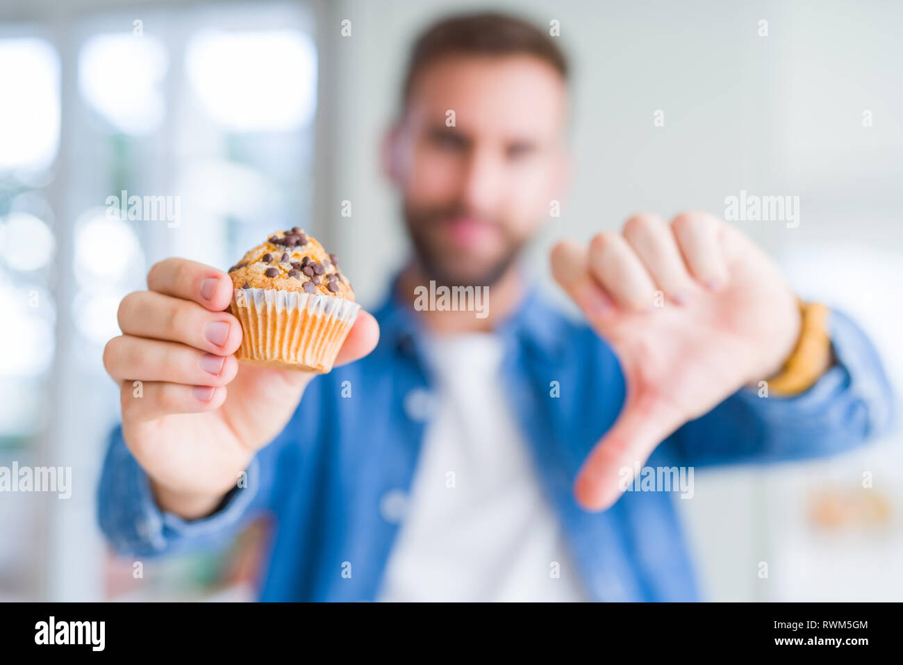Handsome man eating chocolate chips muffin with angry face, negative ...
