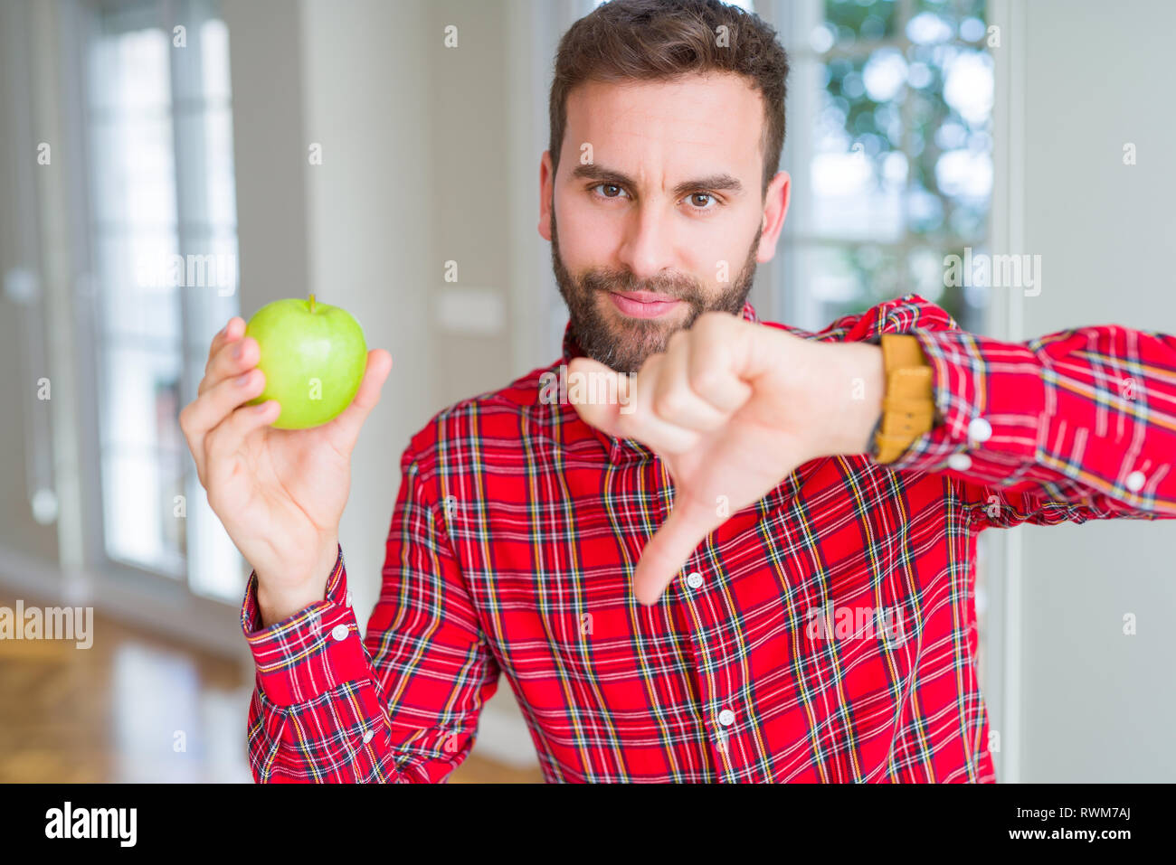 Handsome man eating fresh healthy green apple with angry face, negative ...