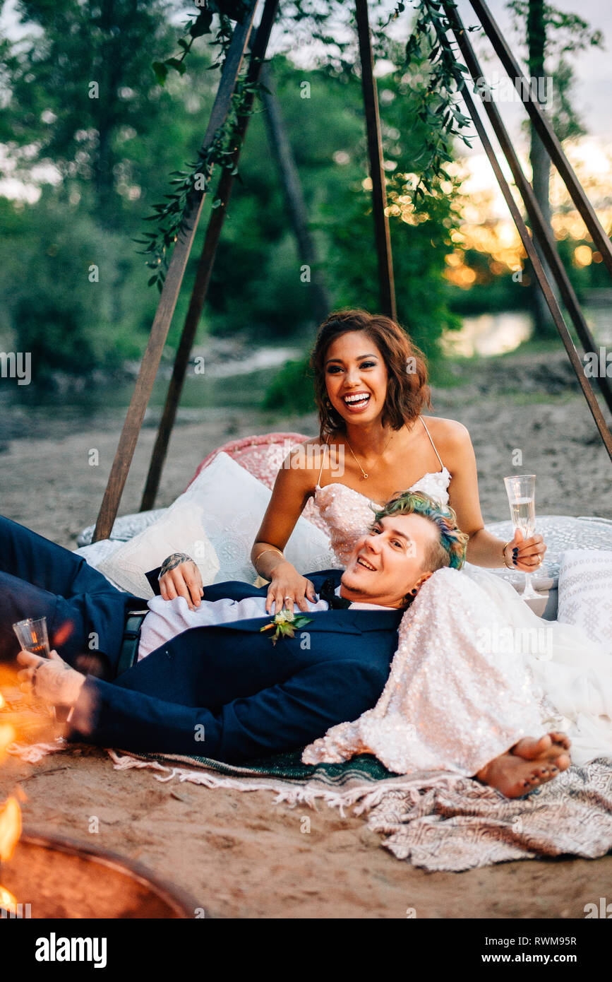 Bride and groom reclining by campfire on lakeside Stock Photo - Alamy