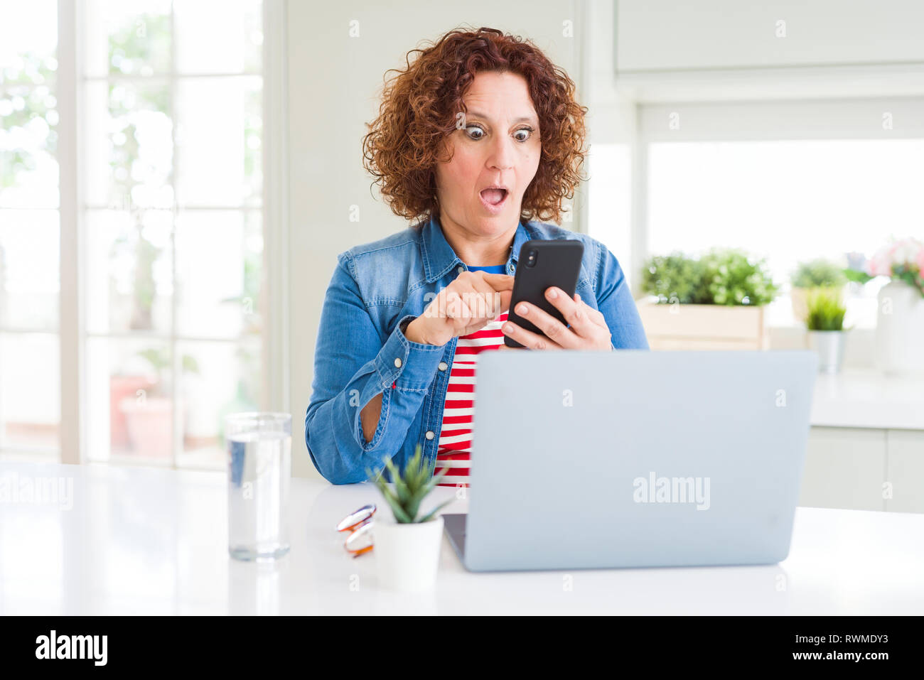 Senior woman using laptop and smartphone scared in shock with a ...