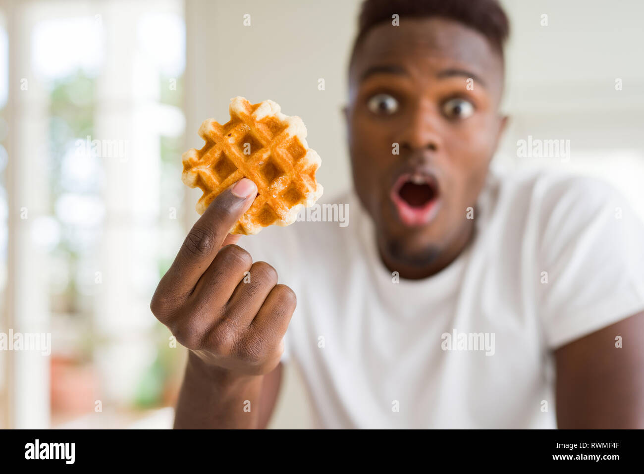 African american man eating sweet Belgian waffle scared in shock with a ...