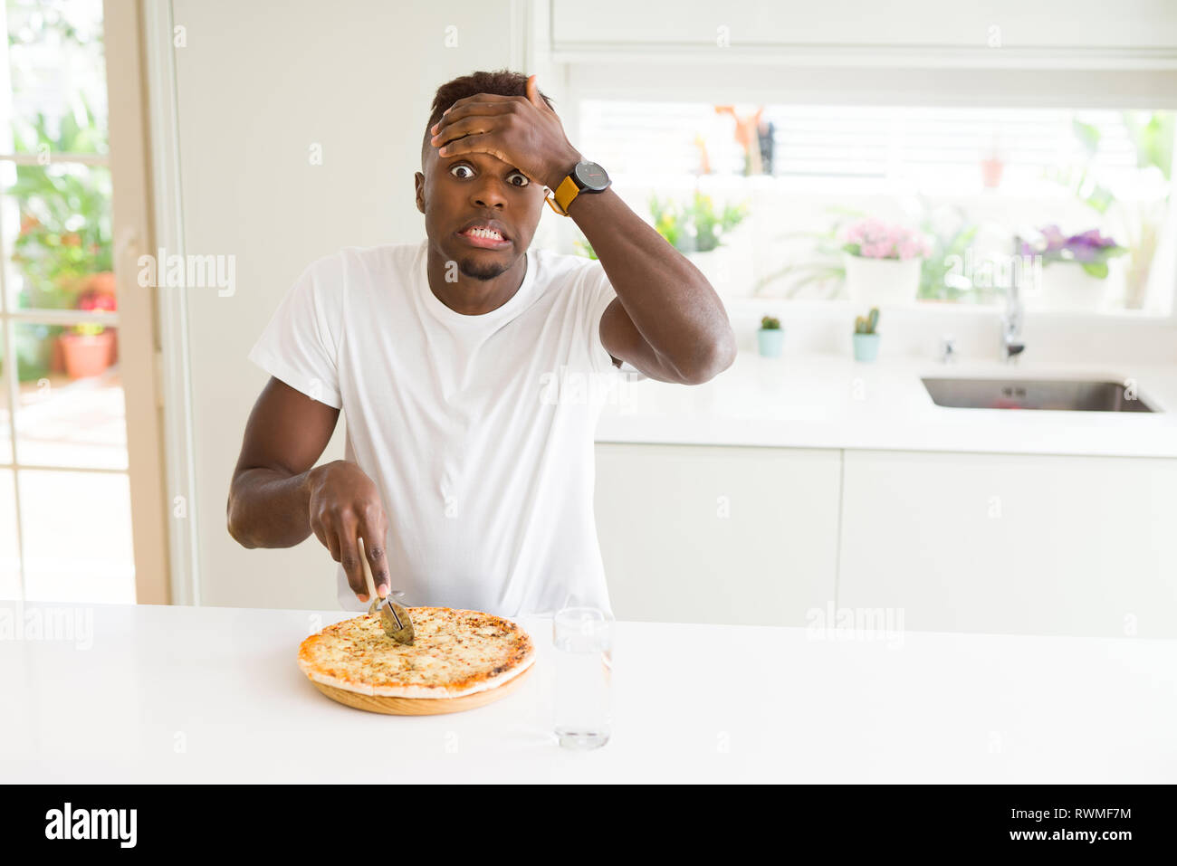 African american man eating cheese pizza at home stressed with hand on ...