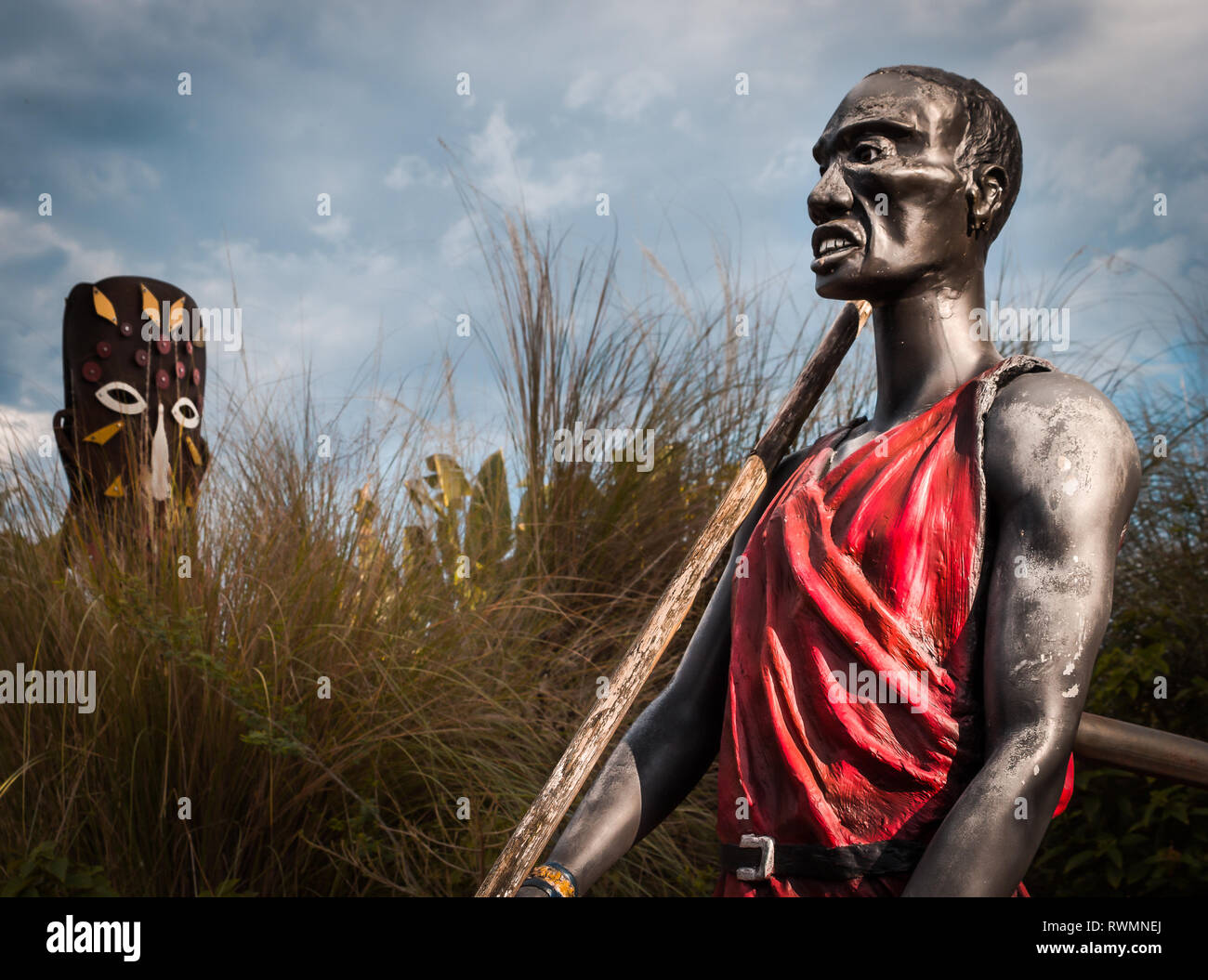 Sculpture of an african person standing by an african mask holding a ...