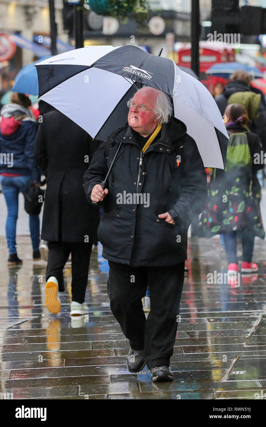 A man is seen sheltering from the rain beneath an umbrella during rainy ...