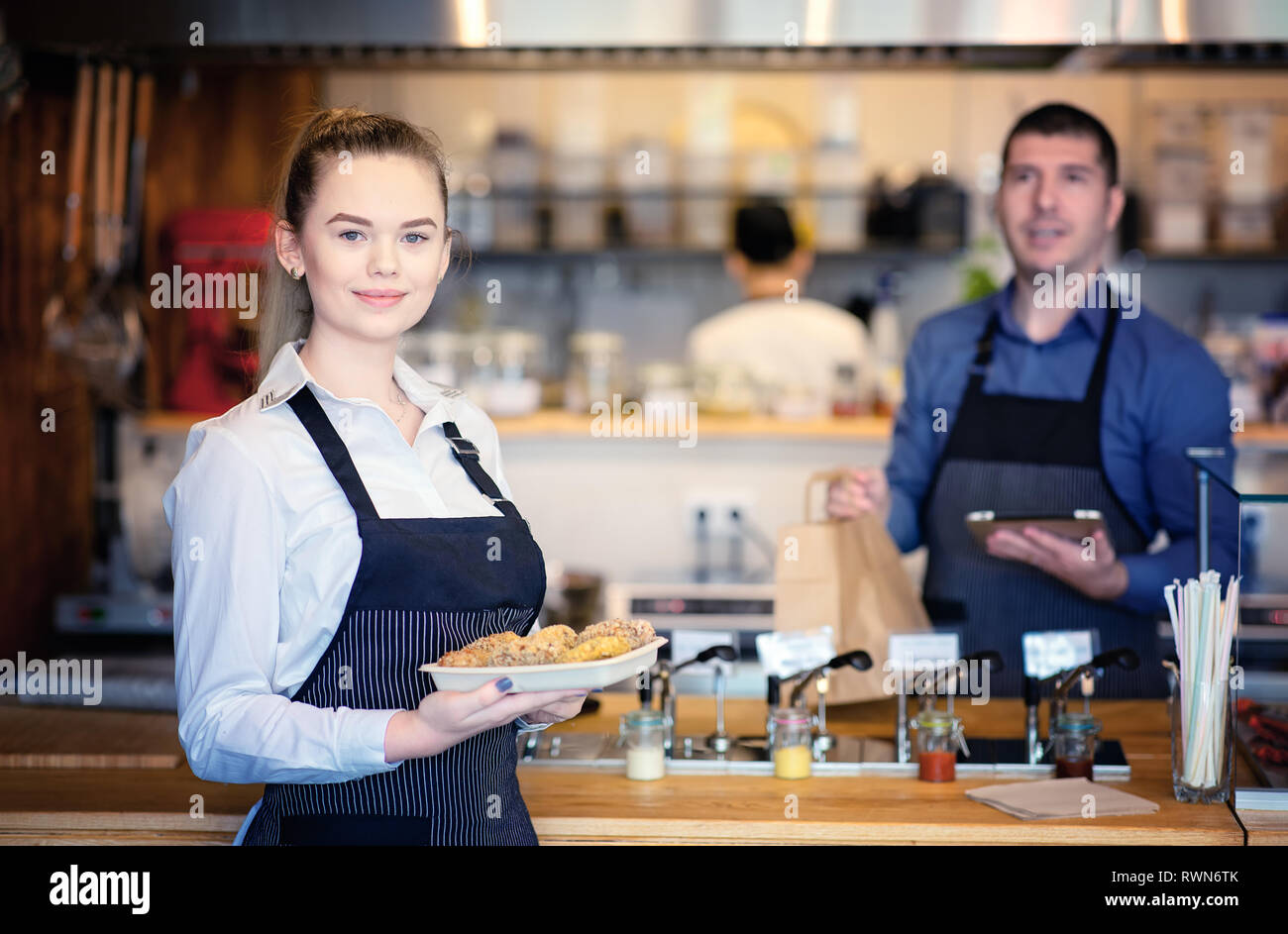 Young woman and man working in a restaurant. Kitchen behind Stock Photo ...