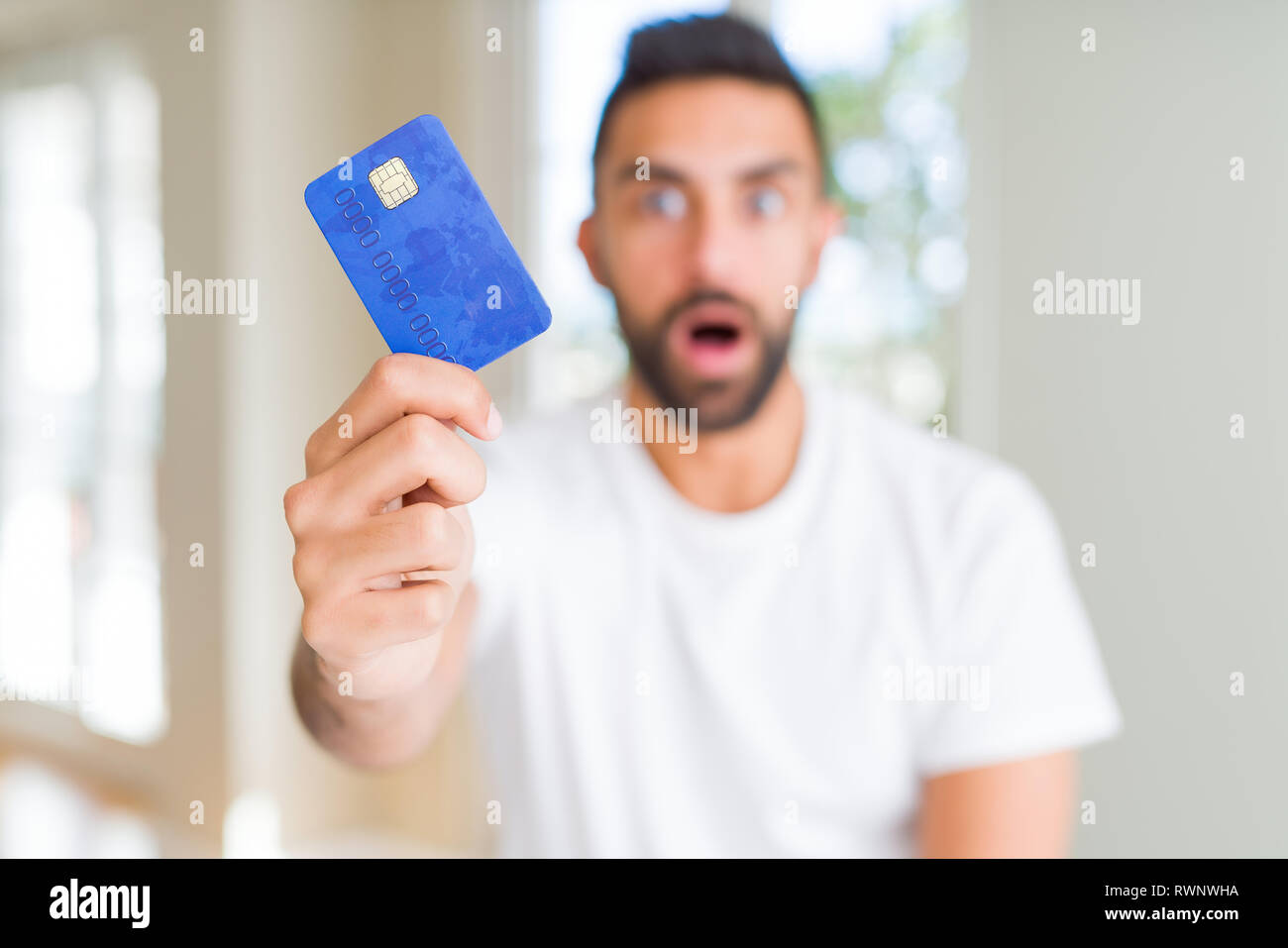Handsome hispanic man holding credit card scared in shock with a ...