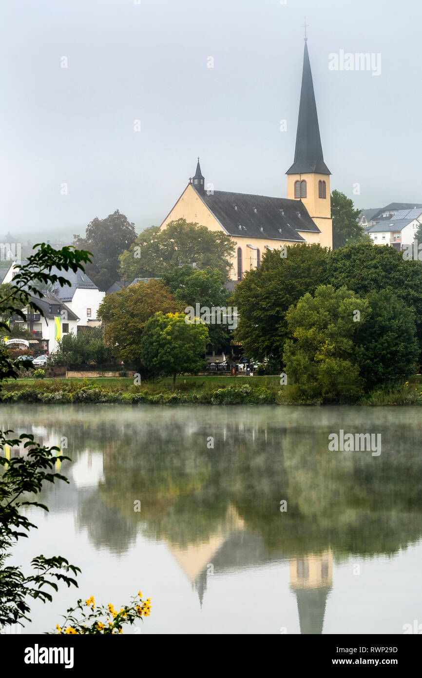 Misty river valley with church in treed area reflecting in the river ...