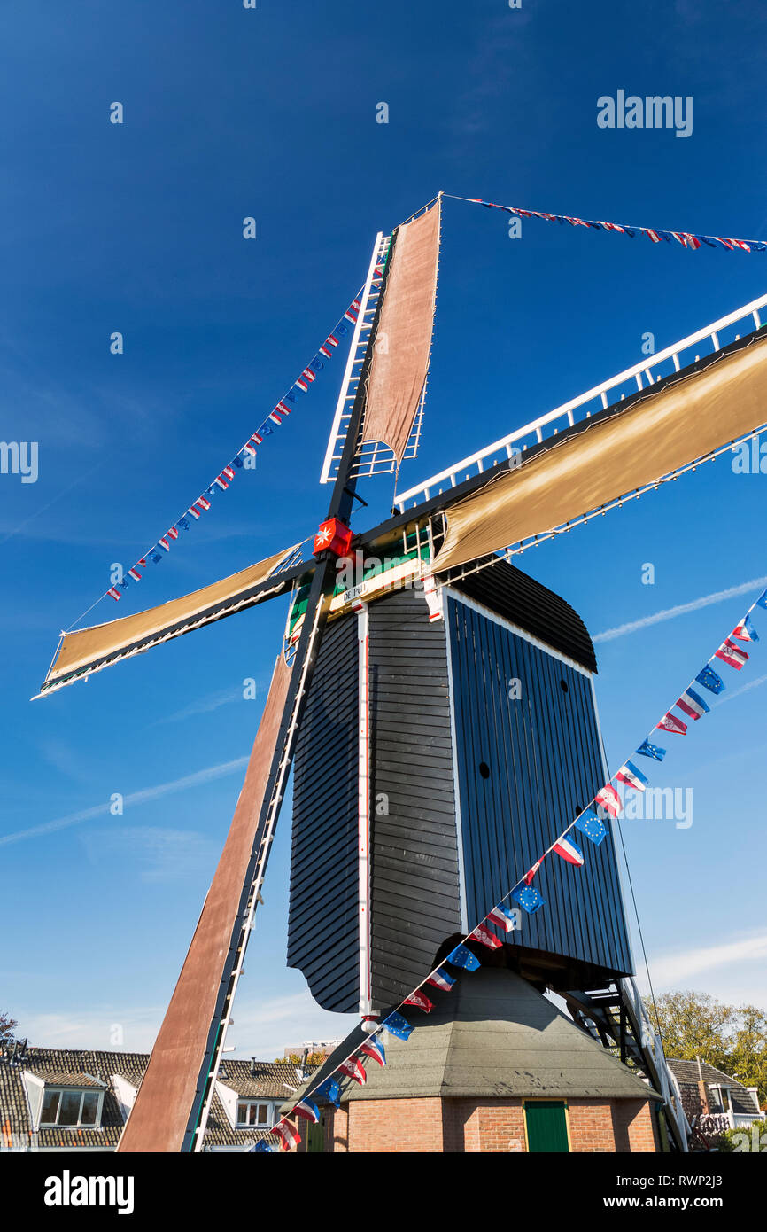 Looking up at old wooden windmill with flagging along it's sails and ...