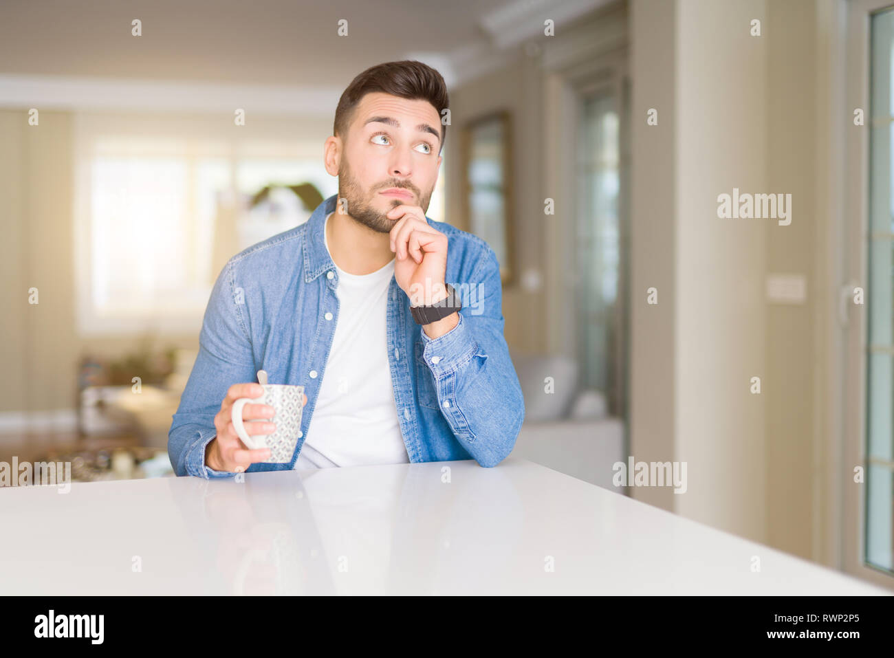 Young handsome man drinking a cup of coffee at home serious face ...