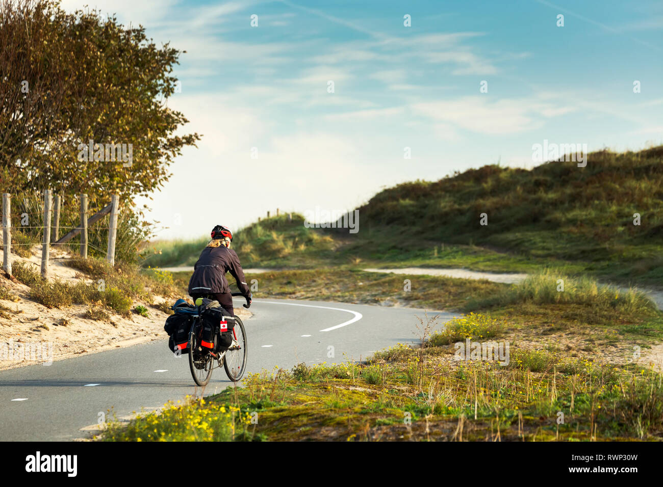 Female cyclist on paved bike pathway along rolling sand dunes and ...