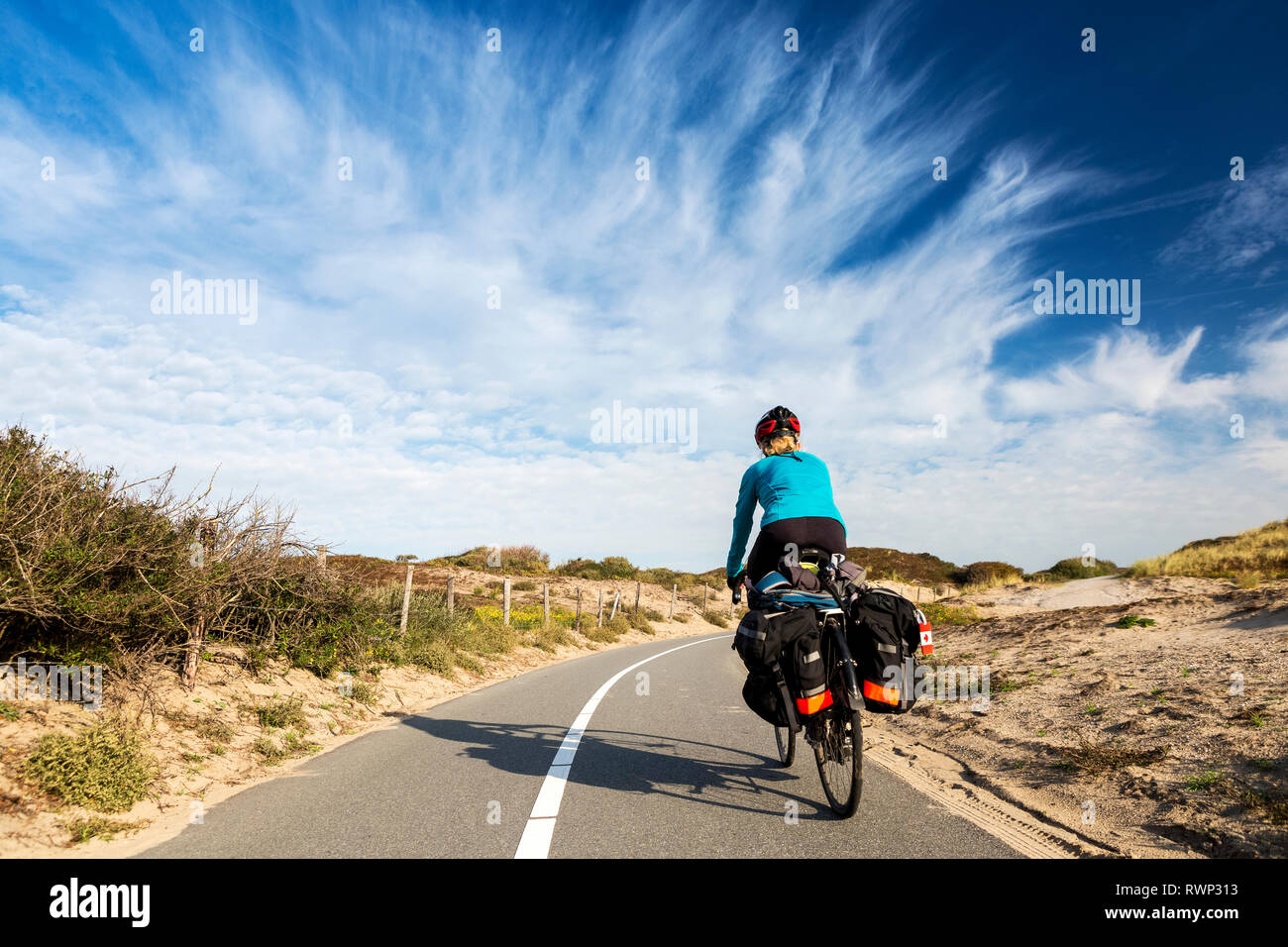Female cyclist on paved bike pathway along rolling sand dunes with ...