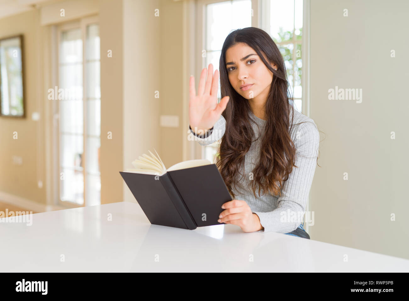 Young woman reading a book with open hand doing stop sign with serious ...