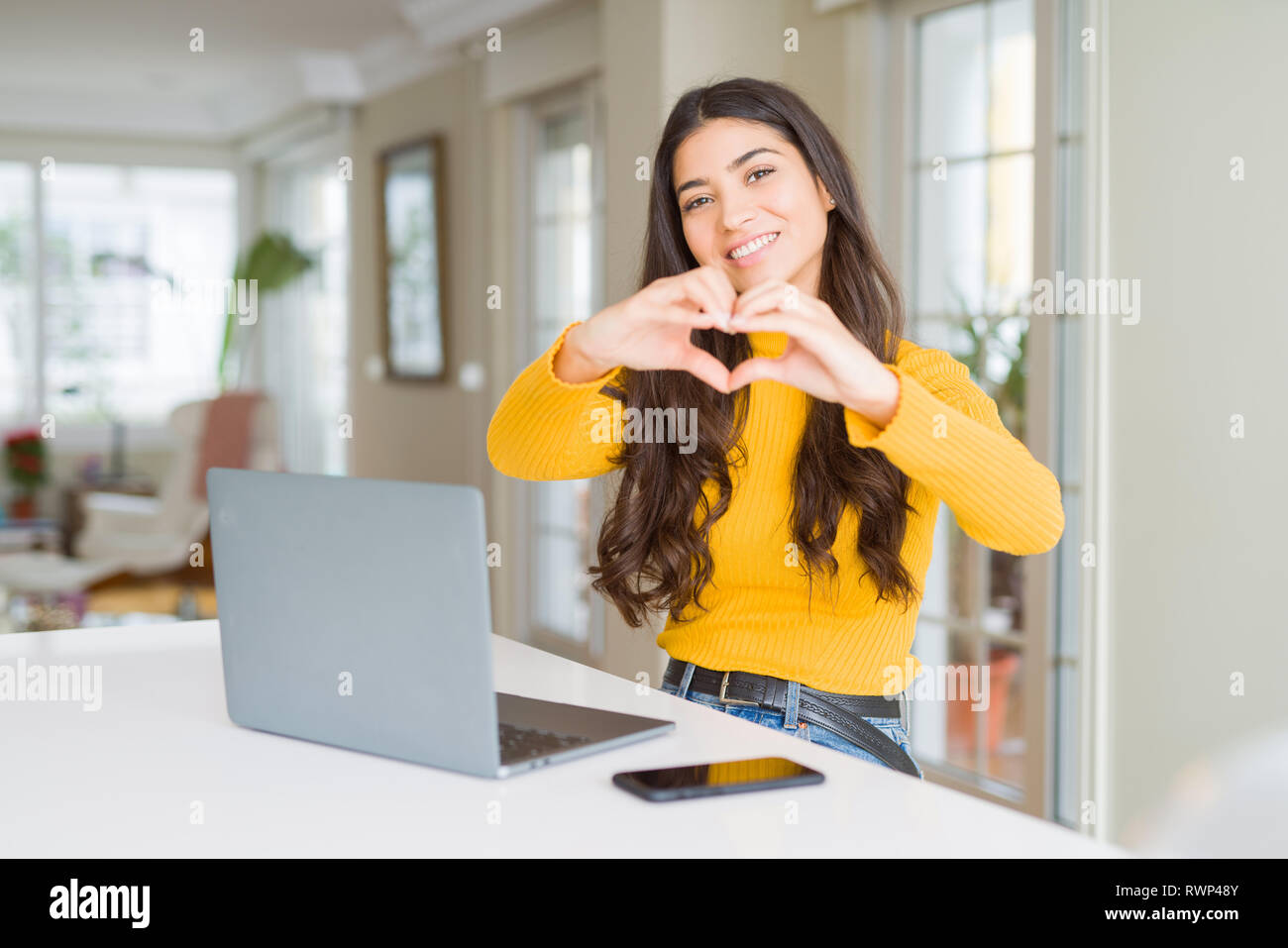 Young woman using computer laptop smiling in love showing heart symbol ...
