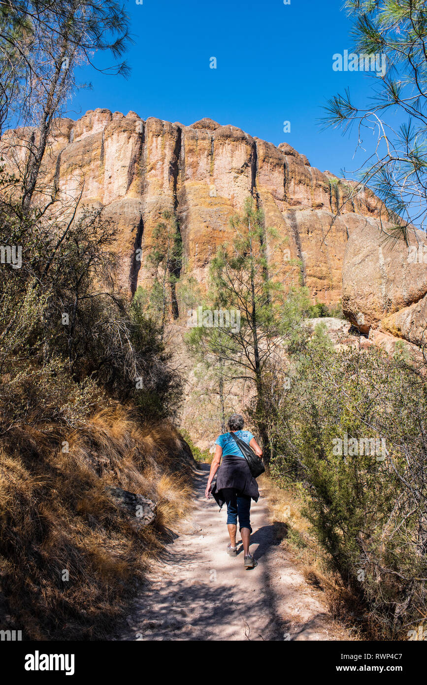 A woman walking up the Balconies Cave trail below massive cliffs in the ...