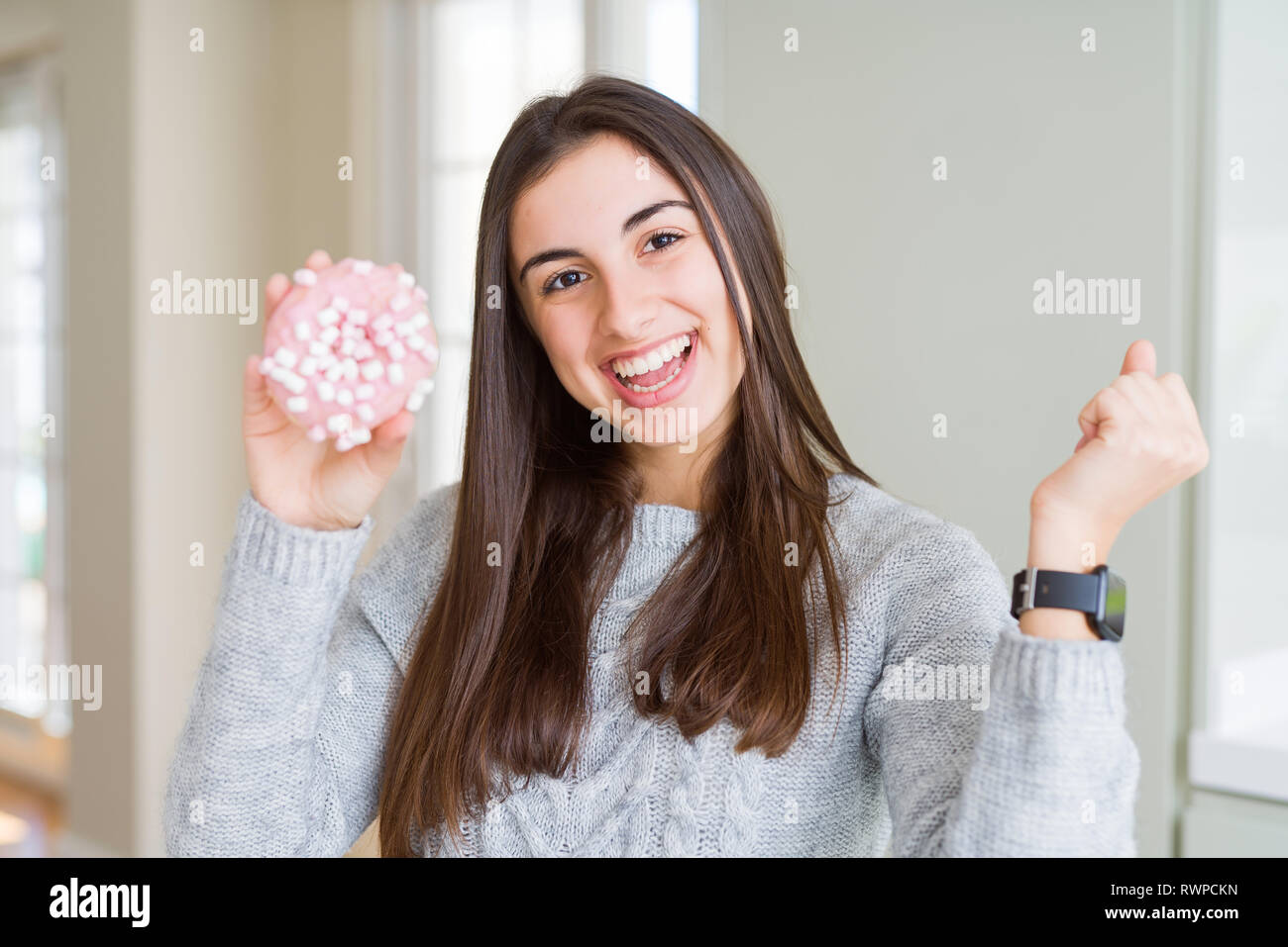 Beautiful young woman eating sugar marshmallow pink donut screaming ...