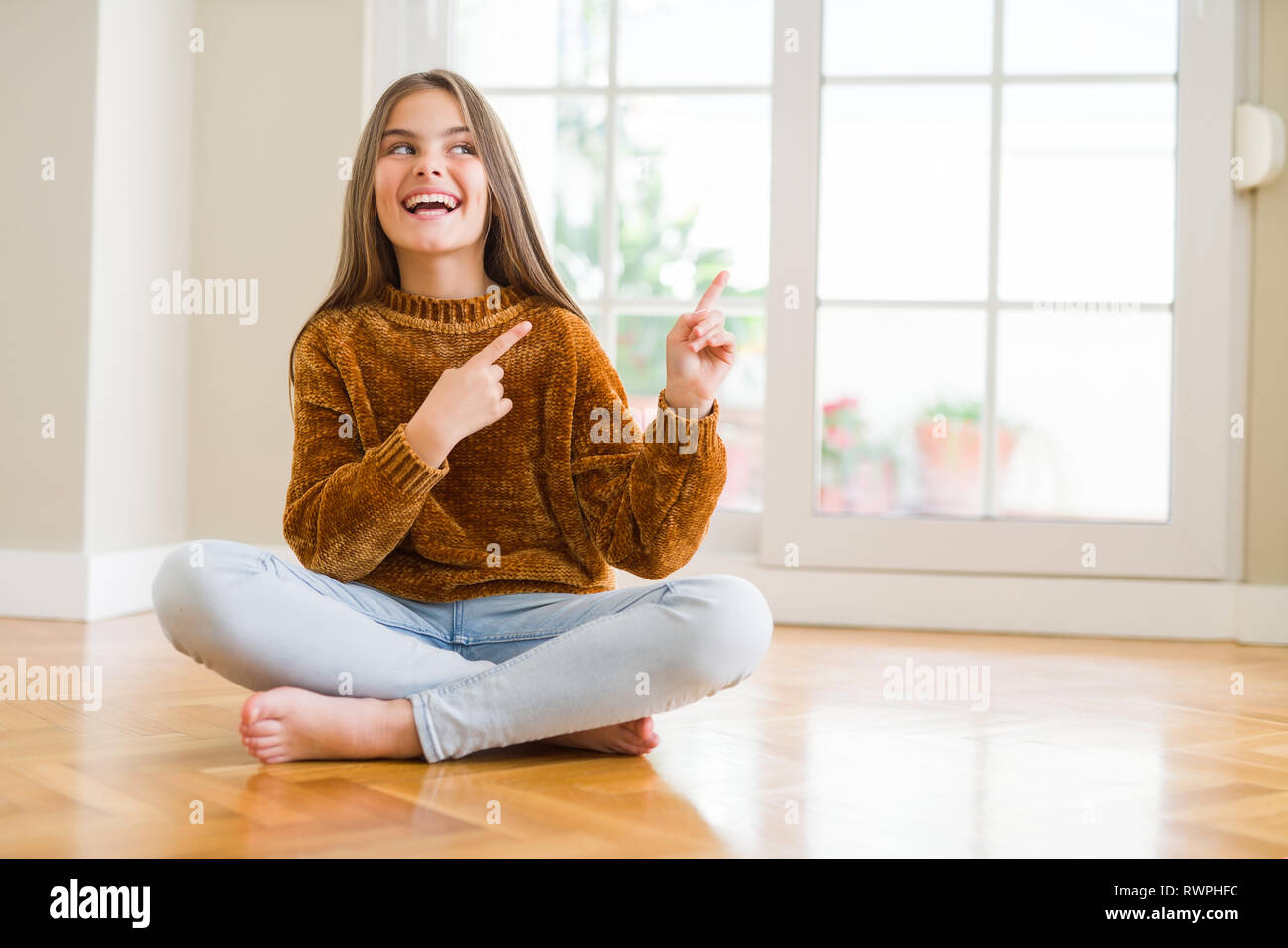 Beautiful young girl kid sitting on the floor at home smiling and ...