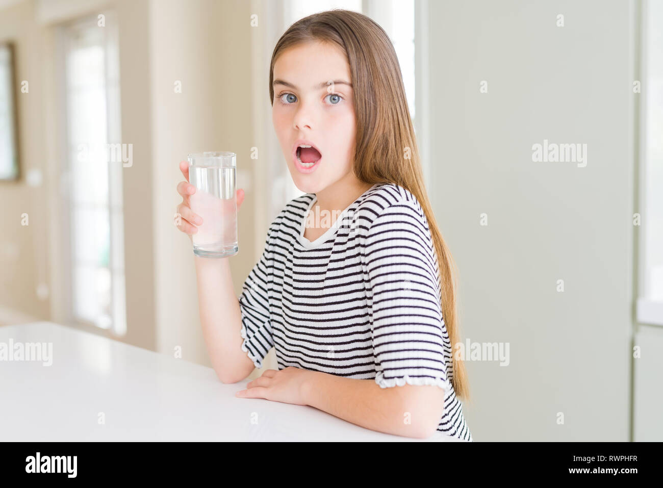 Beautiful young girl kid drinking a fresh glass of water scared in ...