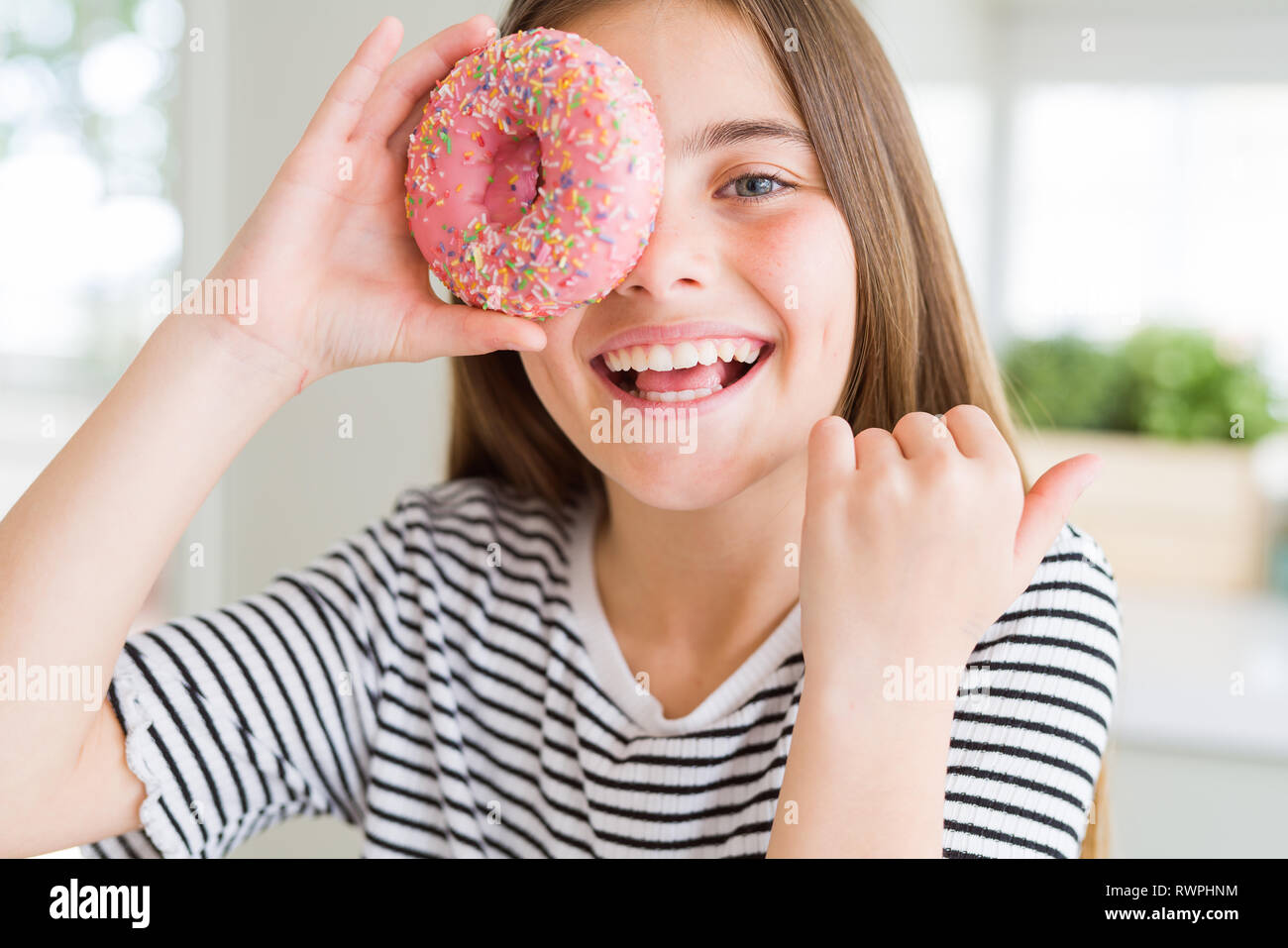 Beautiful young girl kid eating sweet pink donut pointing and showing ...