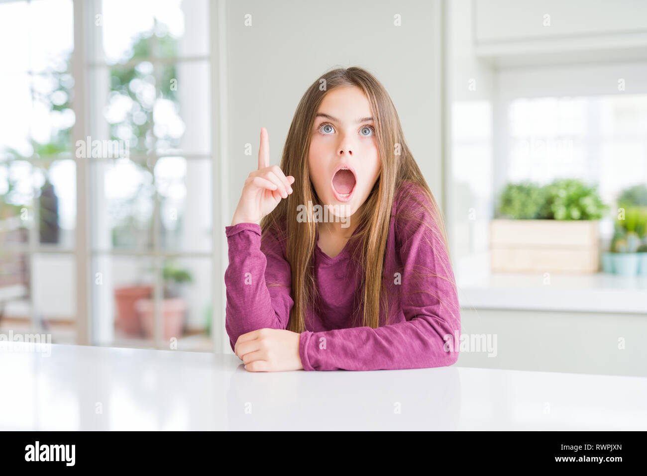 Beautiful young girl kid on white table pointing finger up with ...