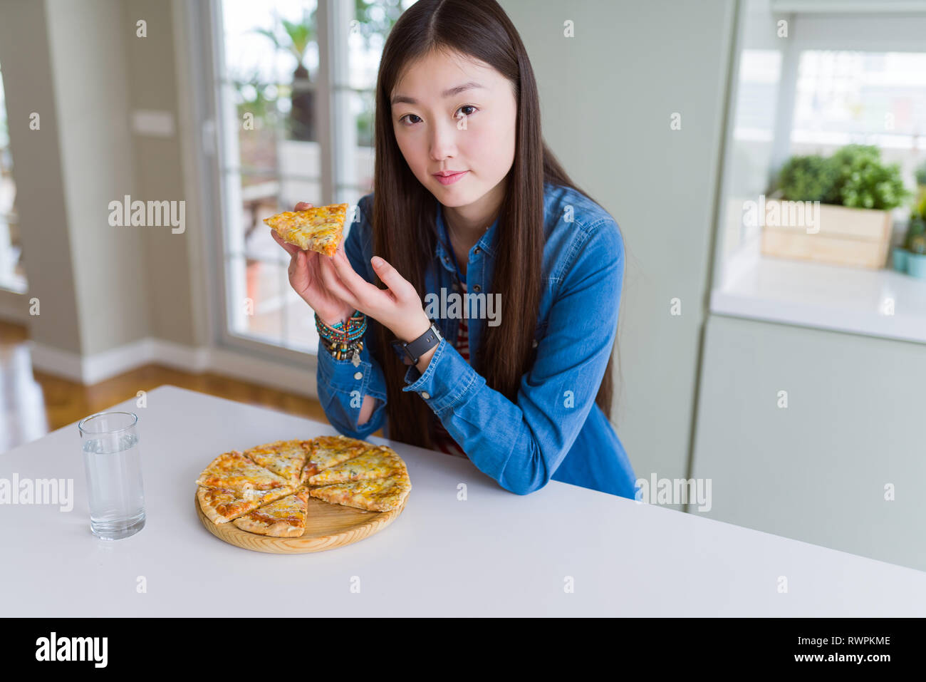 Beautiful Asian woman eating a slice of cheese pizza with a confident ...