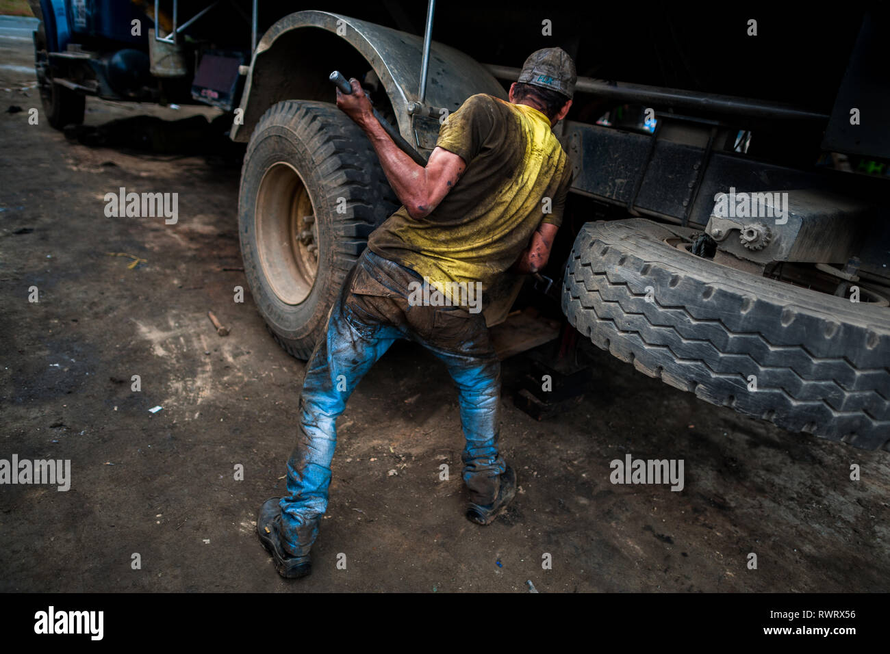 A Colombian car mechanic works with crowbar on a truck’s suspension ...